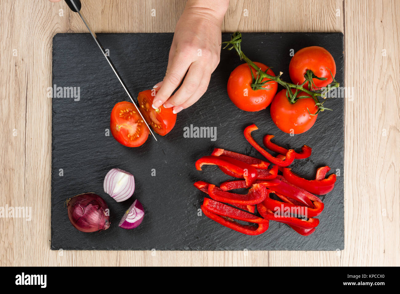 Top down view on black slate cutting board with hands cutting and ...