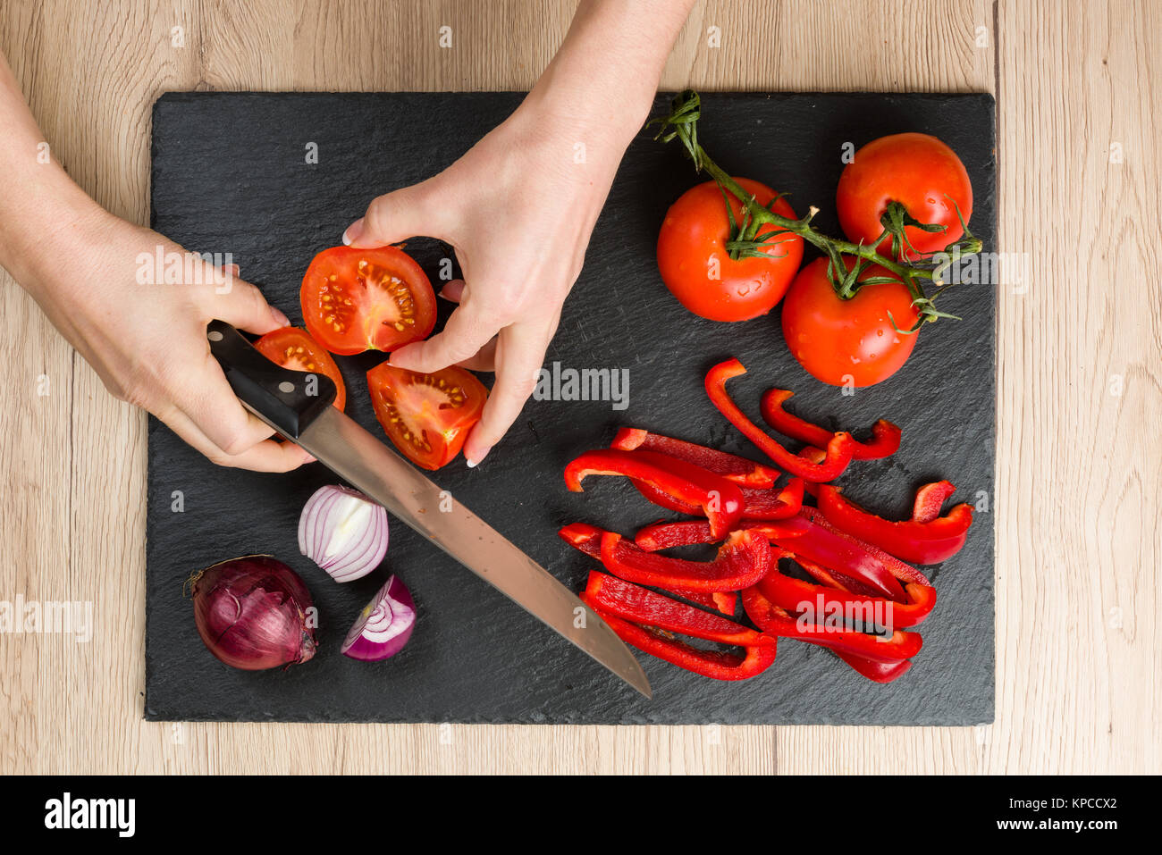 Top down view on black slate cutting board with hands cutting and ...