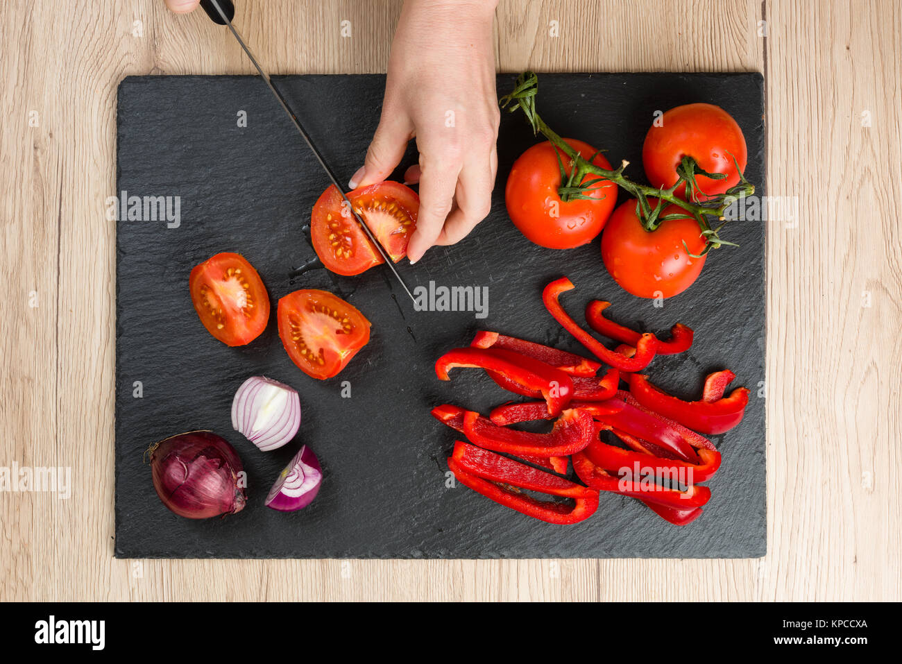 Top down view on black slate cutting board with hands cutting and ...