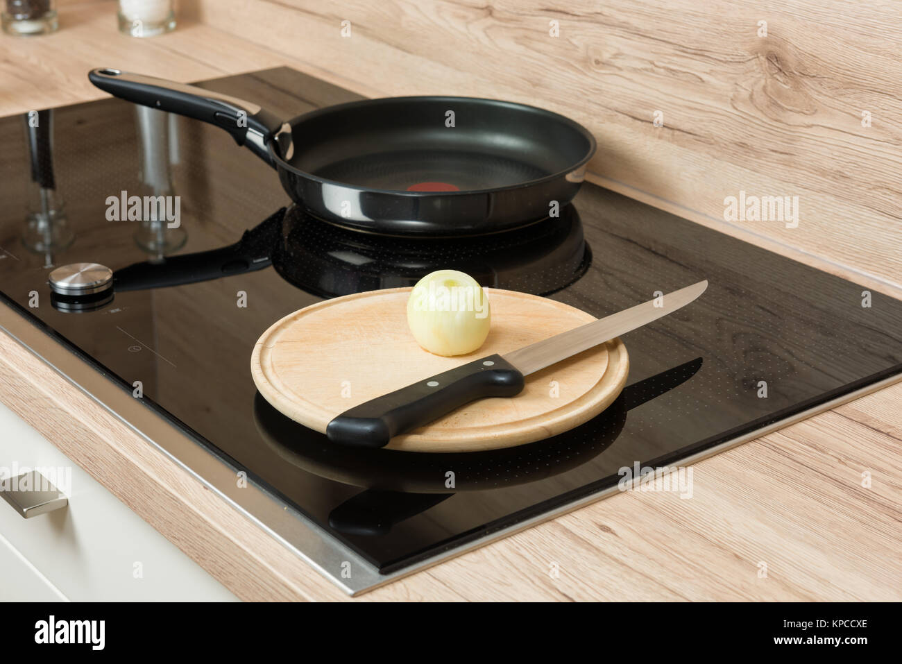 Modern ceramic cooking surface with pan, cutting plate, onion and knife ...