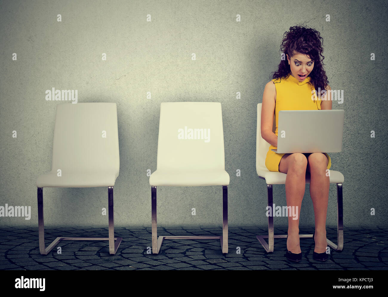 Young woman sitting on chair and browsing laptop with expression of ...