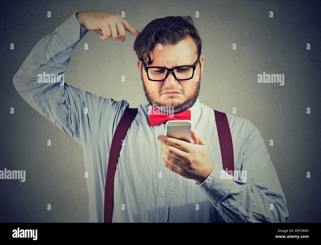 Obese man in eyeglasses looking perplexed while using cellphone on gray ...