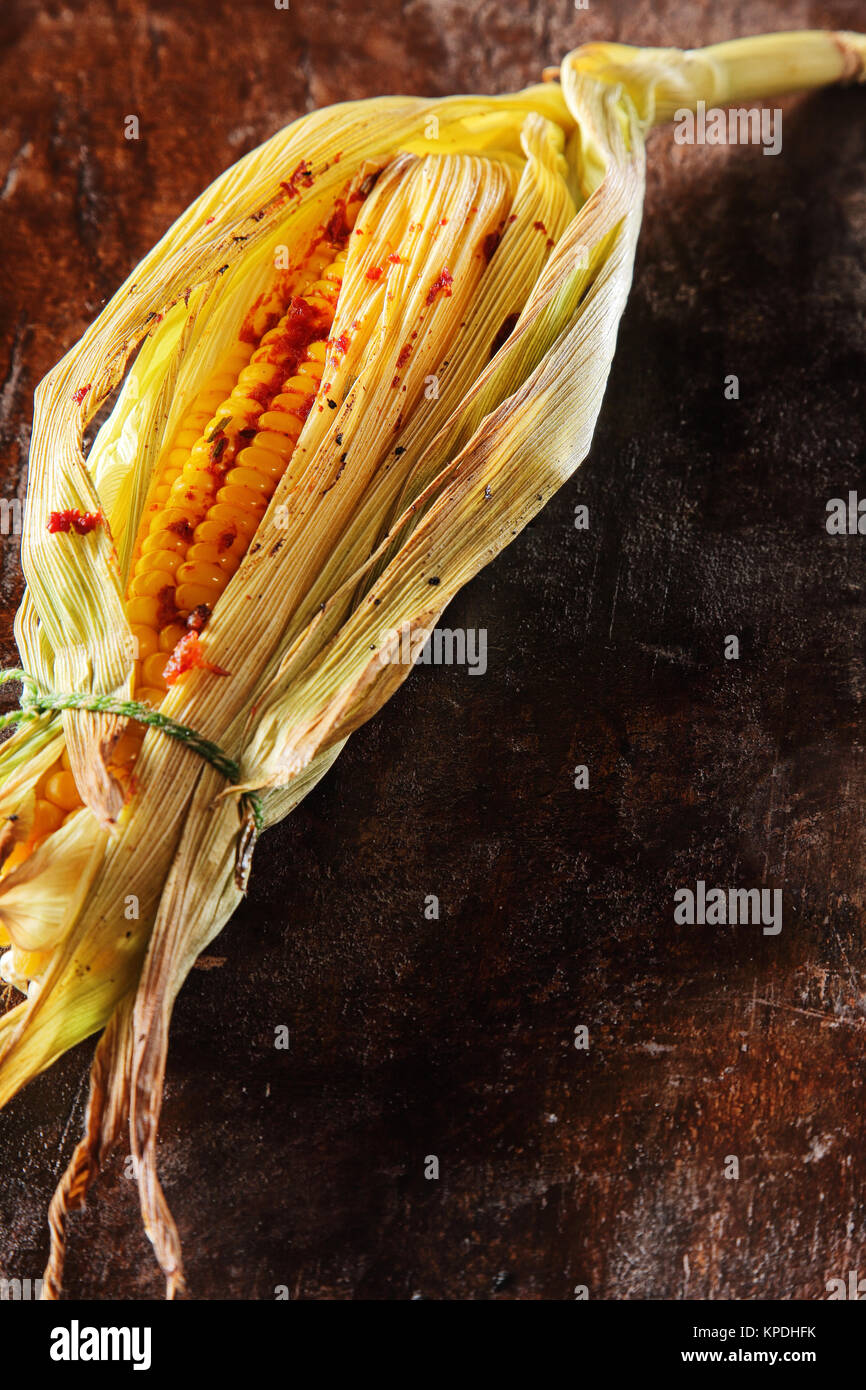 Grilled seasoned corn on the cob tied with green string over a dark ...