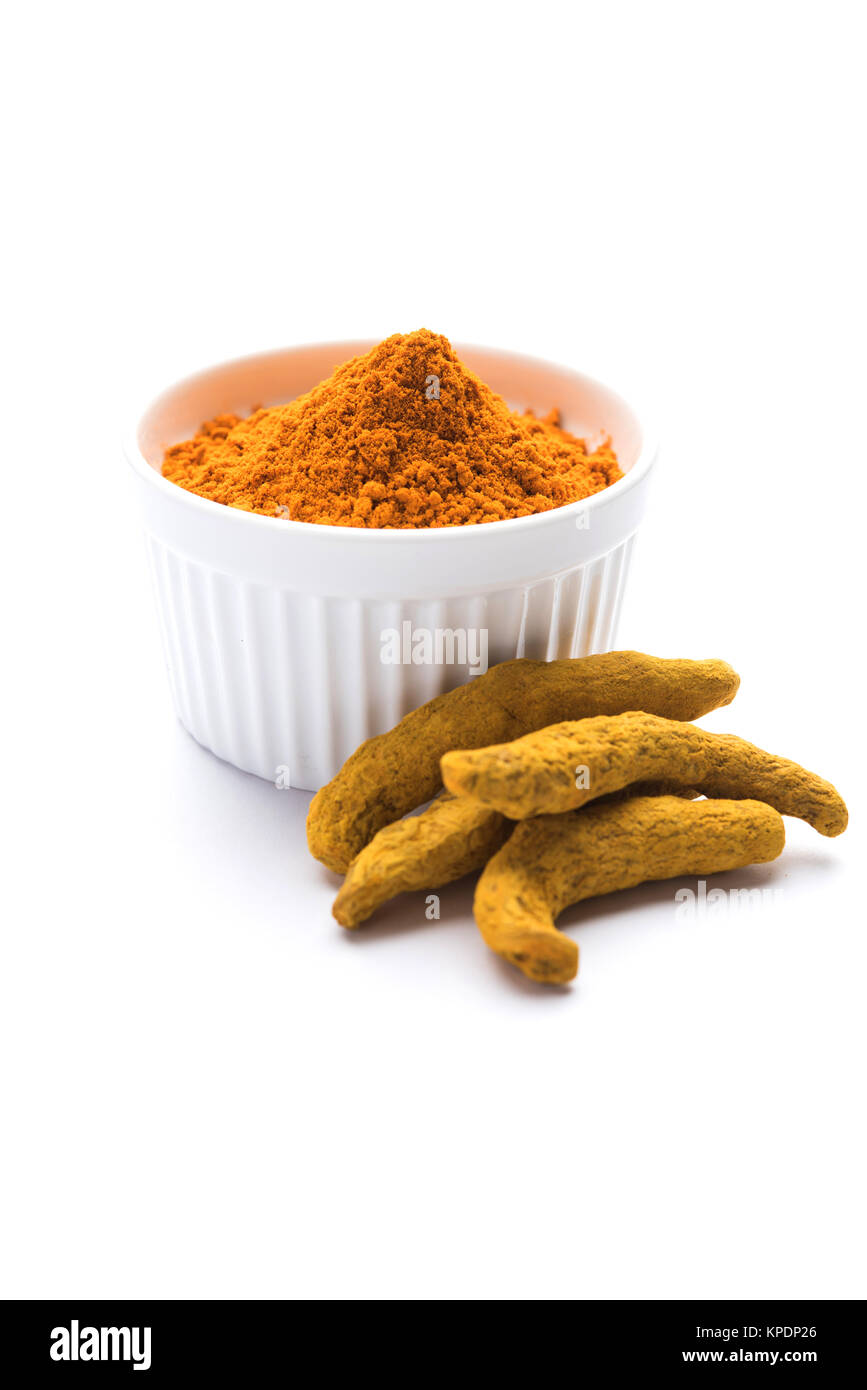 Turmeric powder in ceramic bowl with raw dried turmeric over plain ...