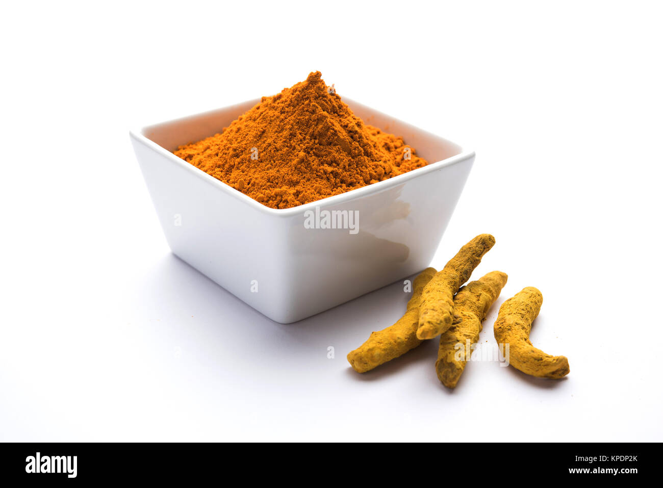 Turmeric powder in ceramic bowl with raw dried turmeric over plain ...