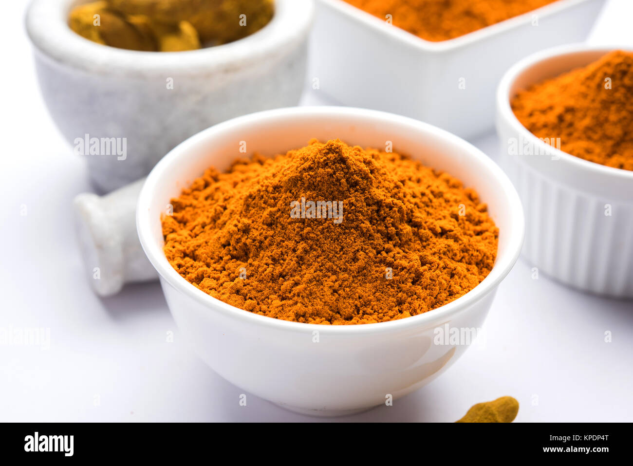 Turmeric powder in ceramic bowl with raw dried turmeric over plain ...