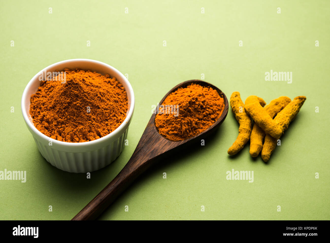 Turmeric powder in ceramic bowl with raw dried turmeric over plain ...