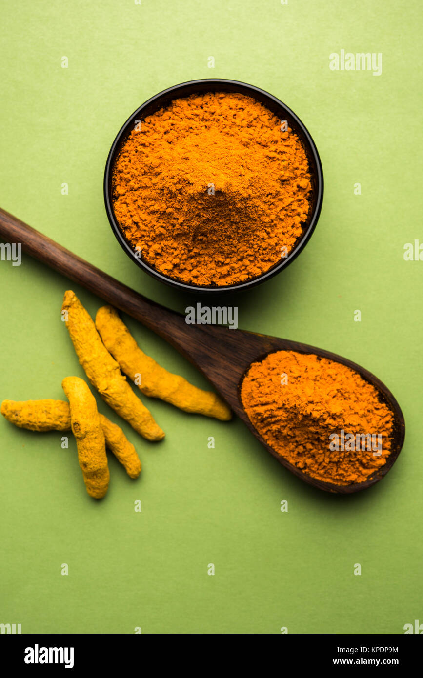 Turmeric powder in ceramic bowl with raw dried turmeric over plain ...