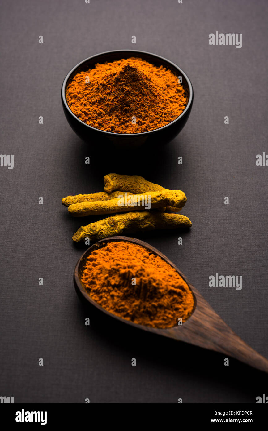Turmeric powder in ceramic bowl with raw dried turmeric over plain ...