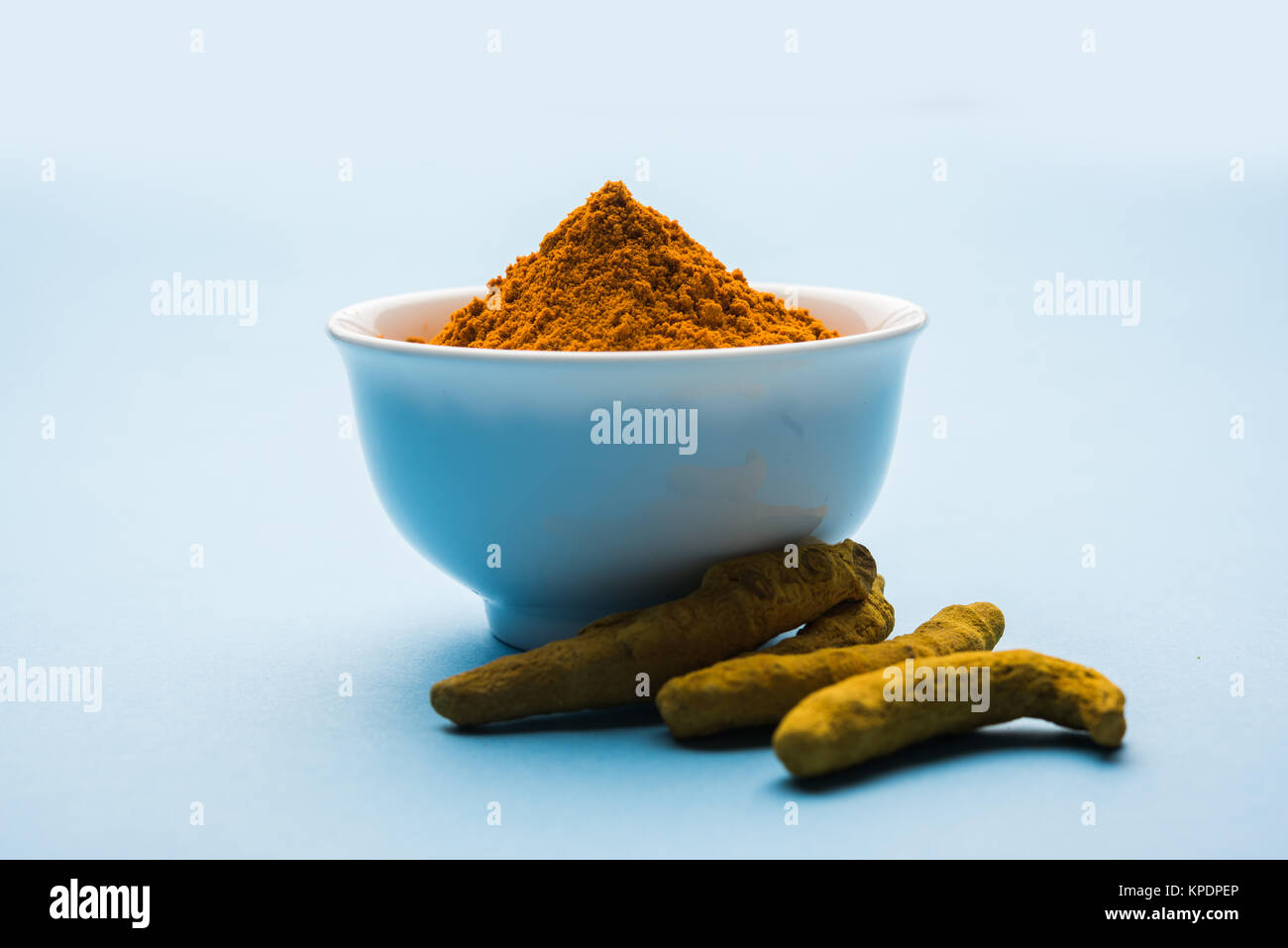 Turmeric powder in ceramic bowl with raw dried turmeric over plain ...