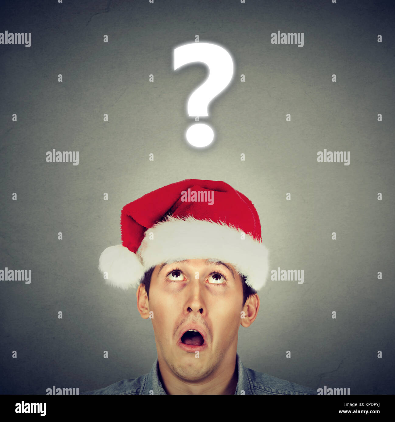 Young man wearing red Santa hat and looking at question mark having no ...