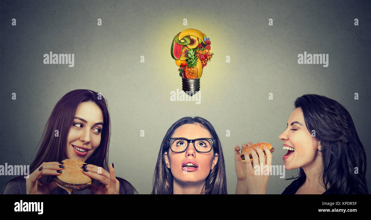 Two women eating hamburgers looking at stressed thoughtful girl with ...