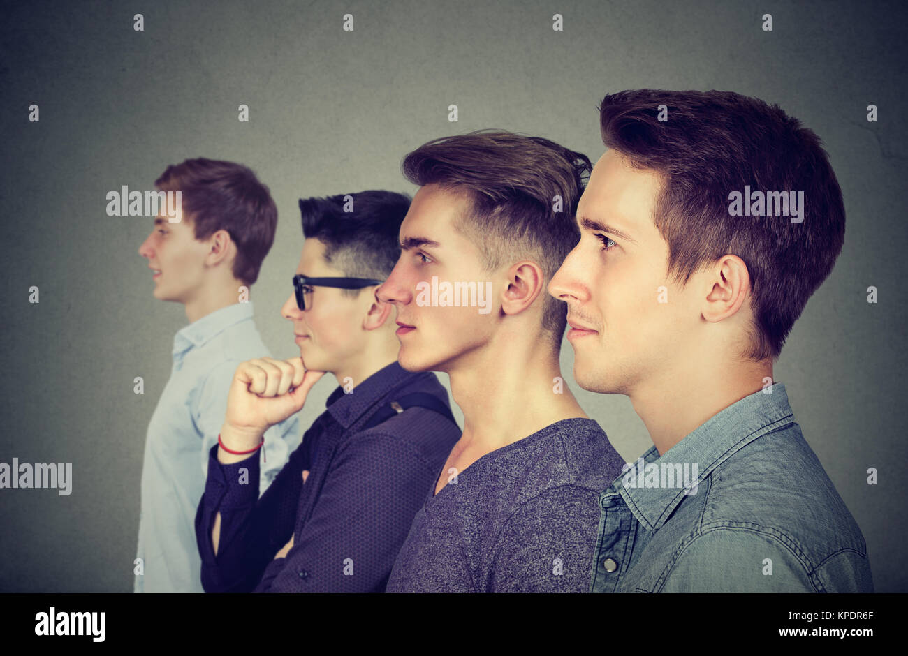 Side view of four young men standing in row and looking forward on gray ...