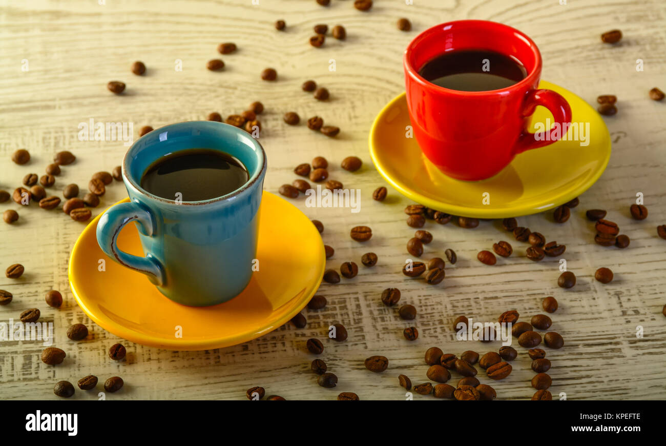 two coffee cups with diferent colors with coffee beans liyng in the ...