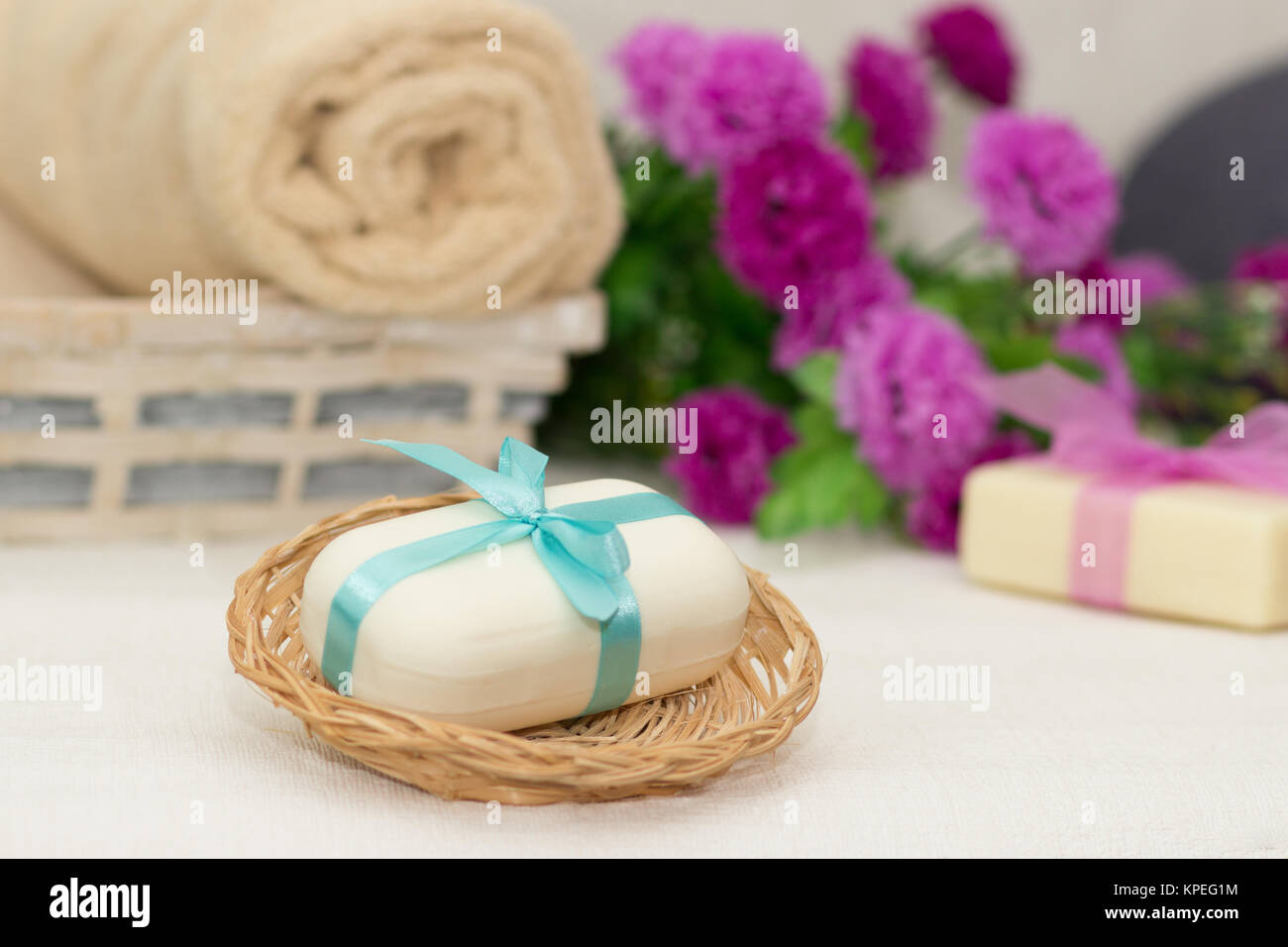 Big piece of beige soap in busket, witn blue bow, flowers and towel on ...