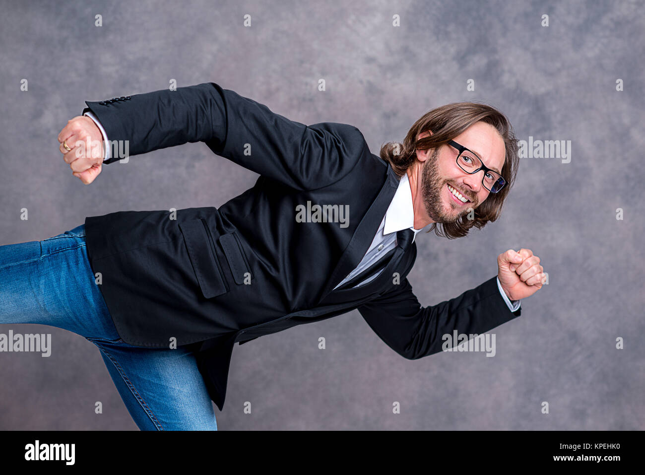 portrait of a young active business man in black suit in front of gray ...