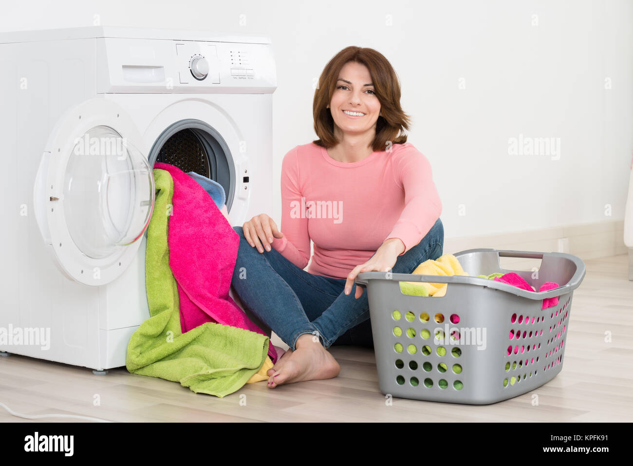 Happy Woman Putting Clothes Into Washing Machine Stock Photo - Alamy