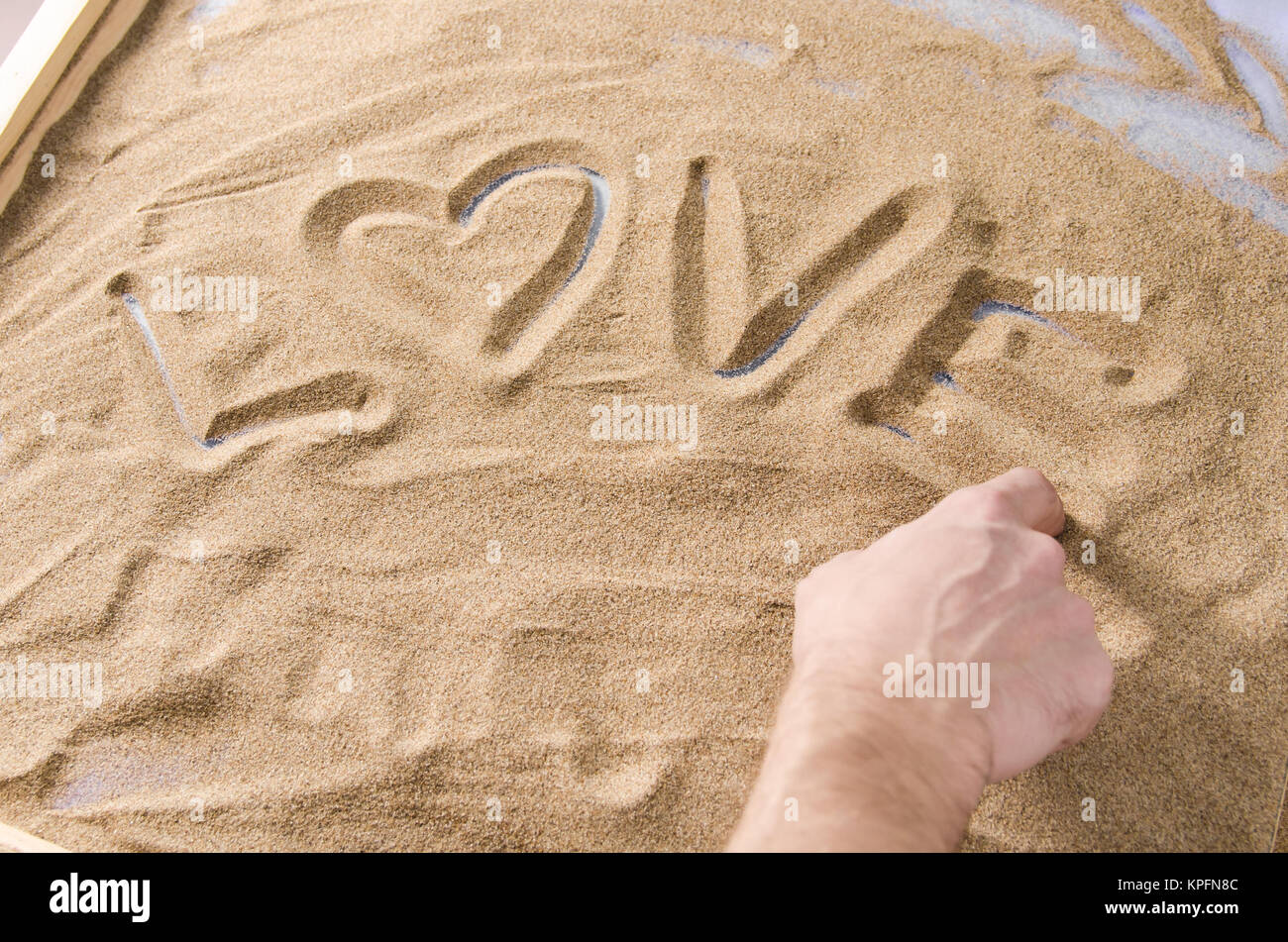 a man draws by his finger on the sand word love with symbol of heart ...