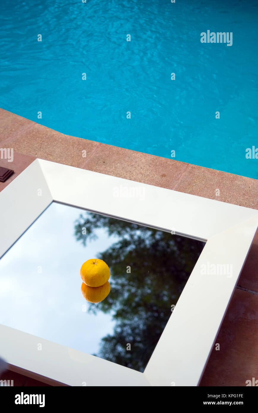a single orange sits on a mirror table by the side of a swimming pool ...