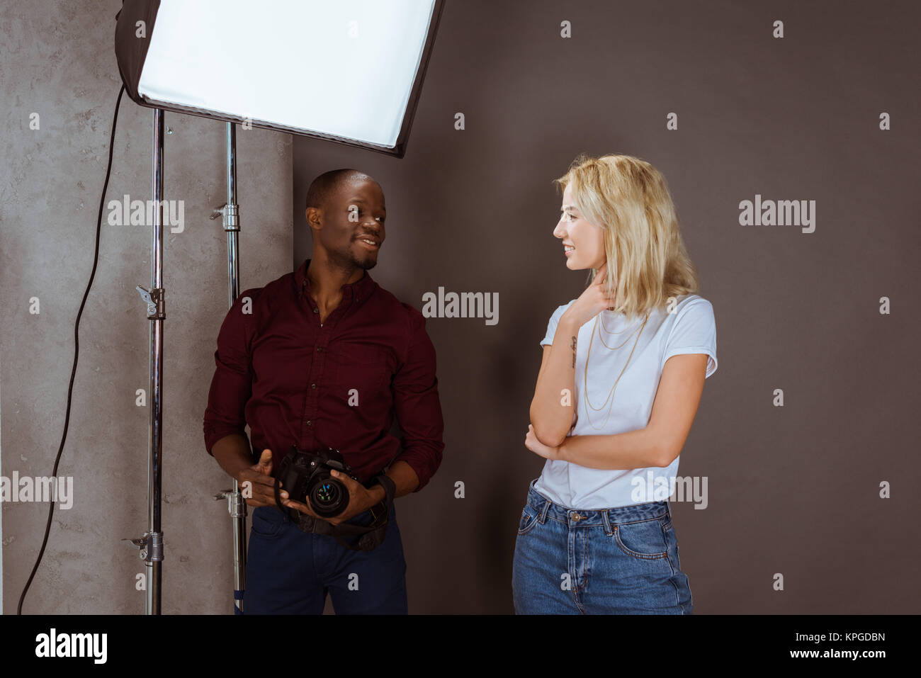 cheerful multiethnic photographer and model looking at each other while ...