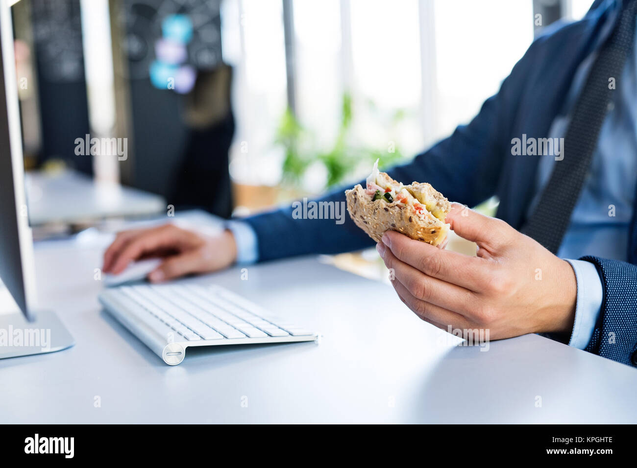 Businessman at the desk with computer eating lunch Stock Photo - Alamy