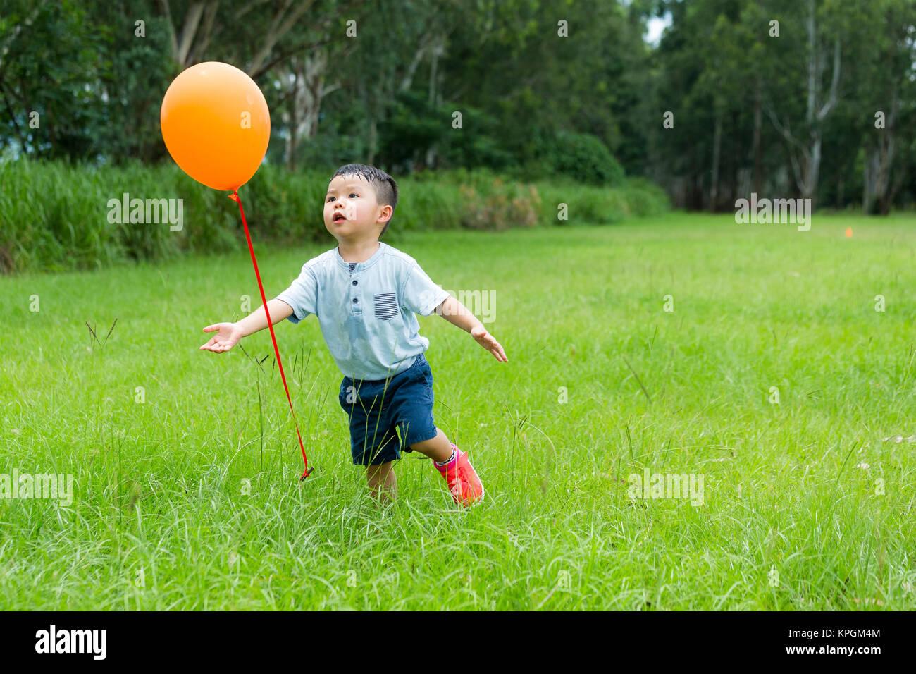 Little boy running to catch with orange balloon Stock Photo - Alamy