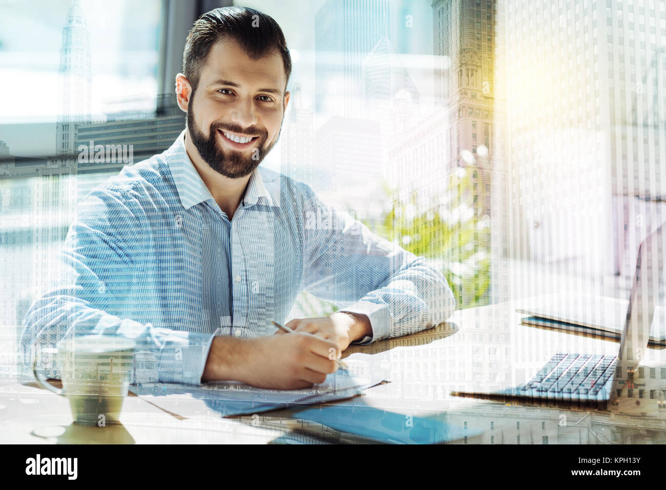 Young smiling man sitting by the table and worksing Stock Photo - Alamy