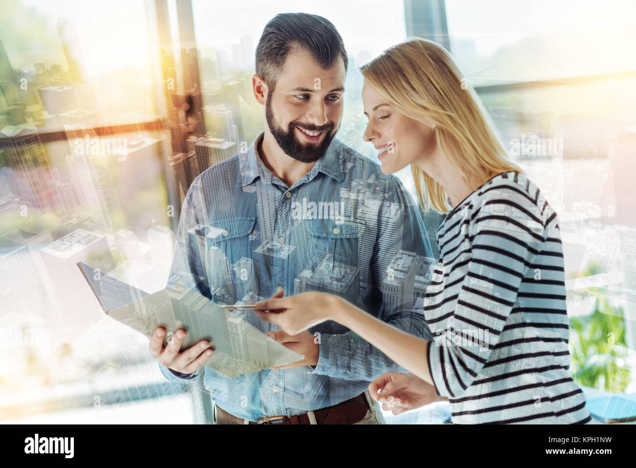 Joyful nice-looking workers standing and working with the notebook ...