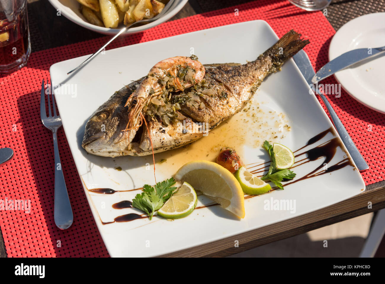 A close up of a freshoy grilled sea bream on a white square plate on a ...
