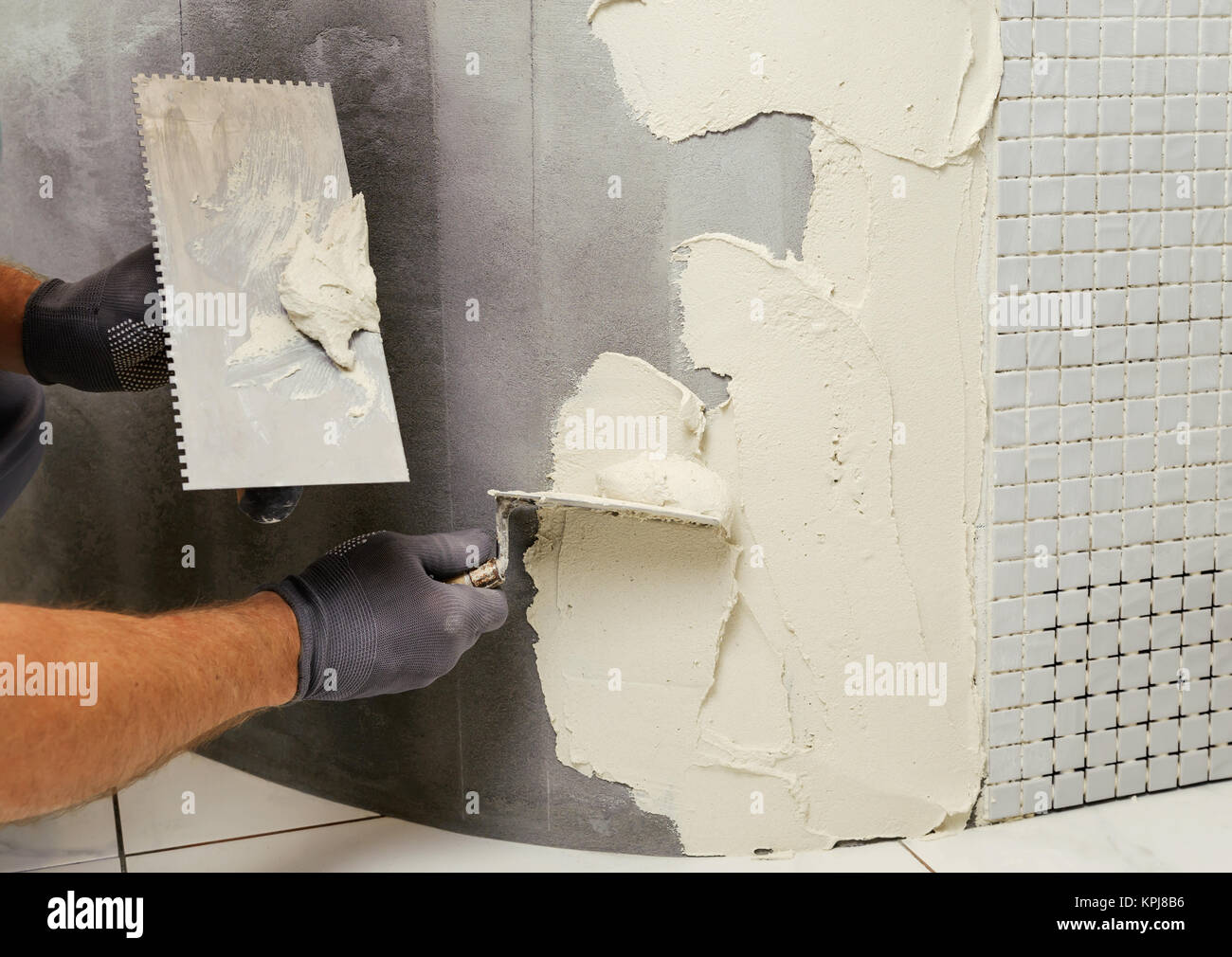Installation of mosaic tiles. The worker puts adhesive on the base ...