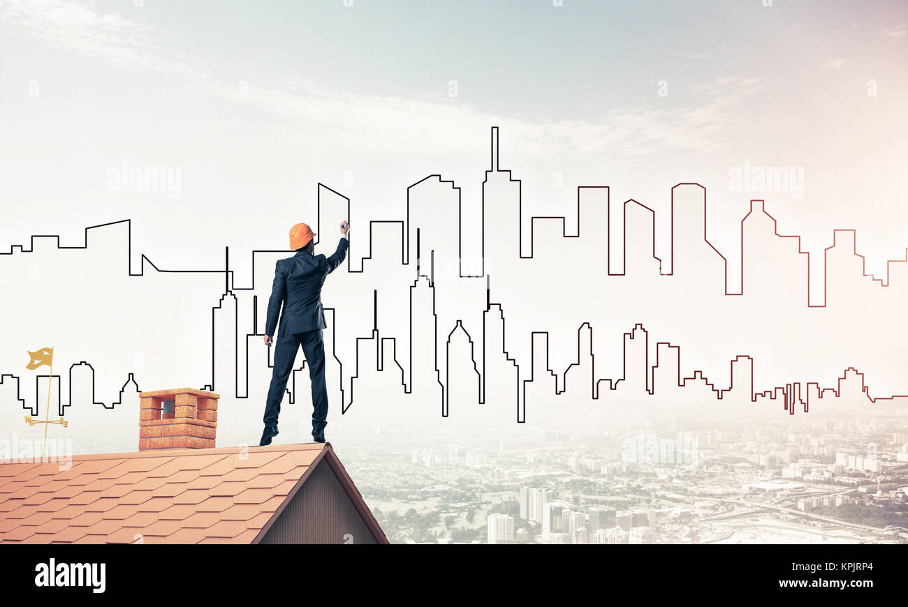 Engineer man standing with back on house roof and drawing city. Mixed ...