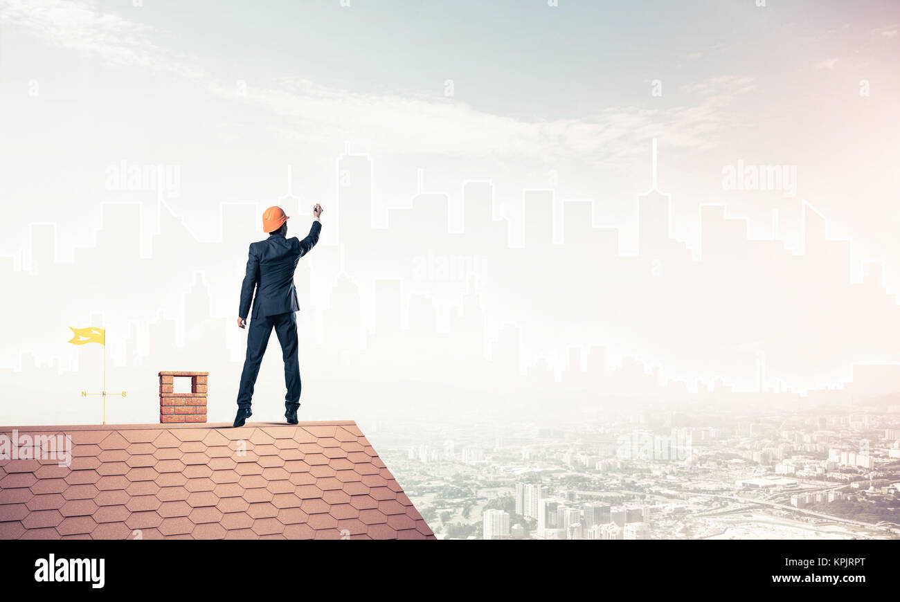 Engineer man standing with back on house roof and drawing city. Mixed ...