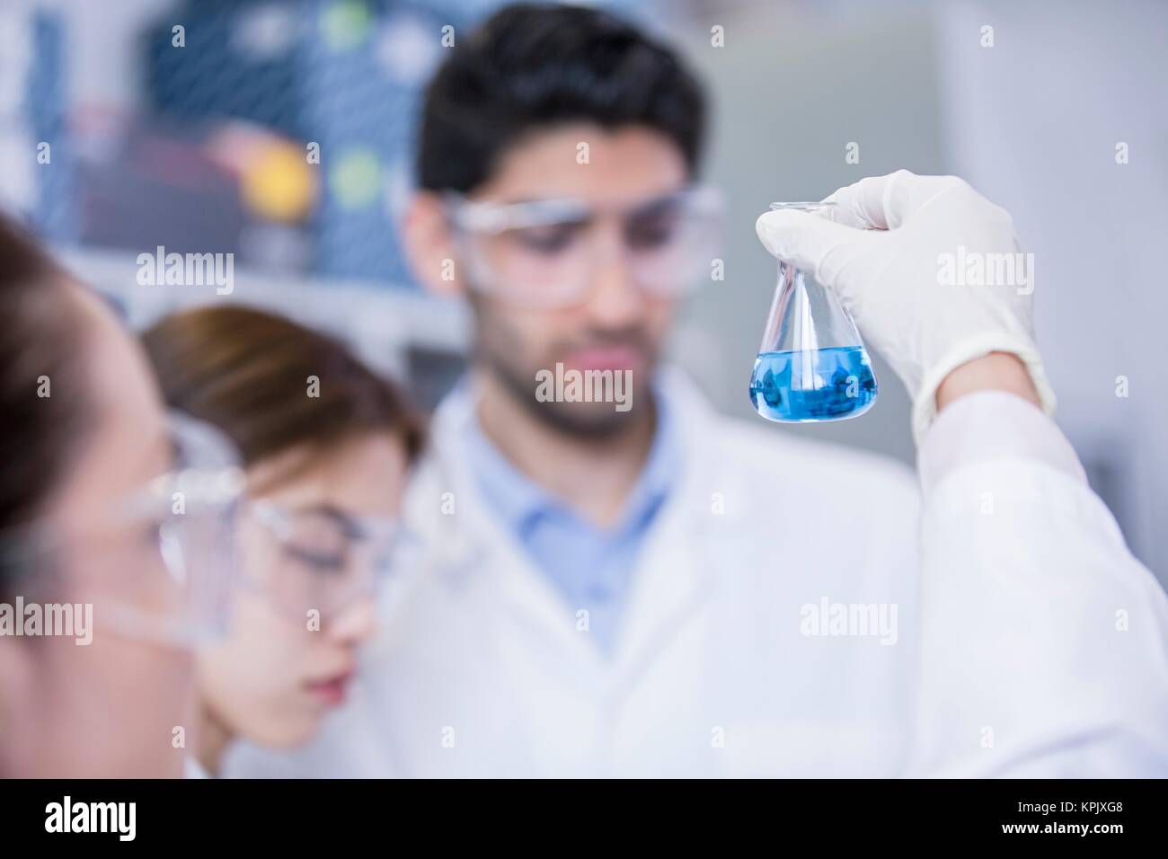 Laboratory assistants looking at chemical flask containing blue liquid ...