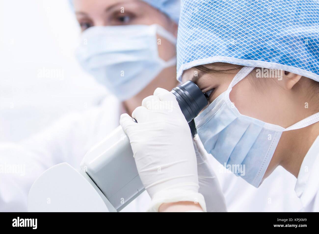 Female scientist wearing protective mask using microscope Stock Photo ...