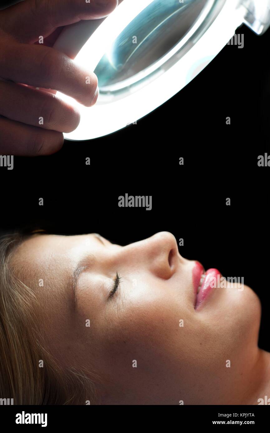 Male doctor examining young woman's face using a daylight magnification ...