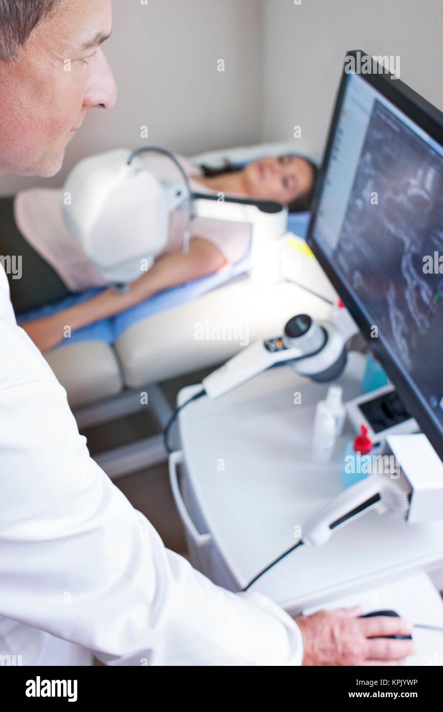 Male doctor looking at computer monitor, female patient on bed. On the ...