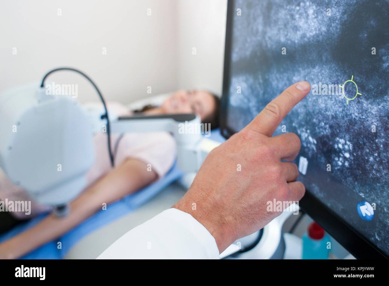 Doctor pointing at computer monitor, female patient on bed. On the ...