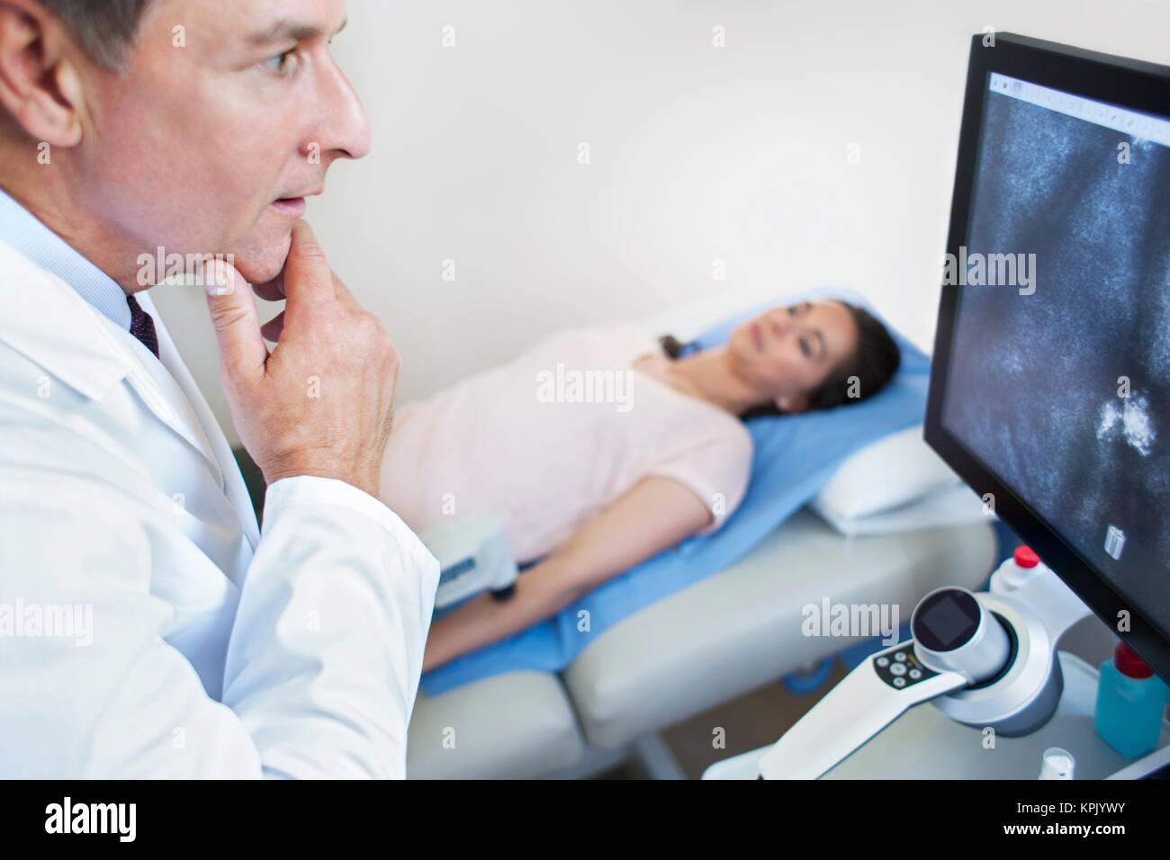 Doctor looking at computer monitor with hand on chin, female patient on ...