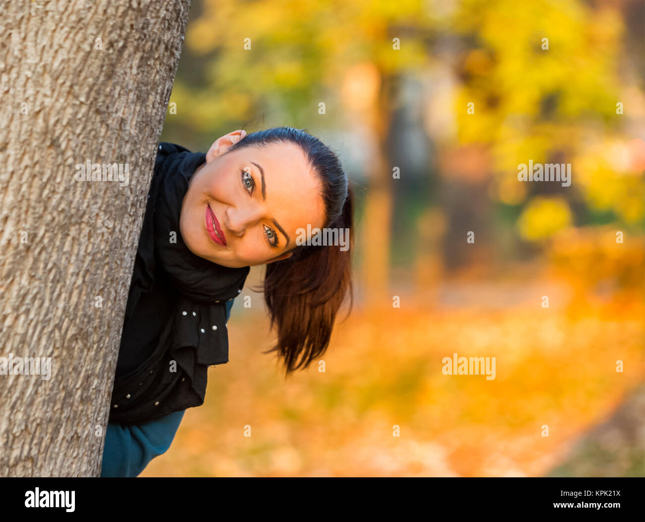 Happy woman hiding behind a tree in a beautiful autumn day Stock Photo ...