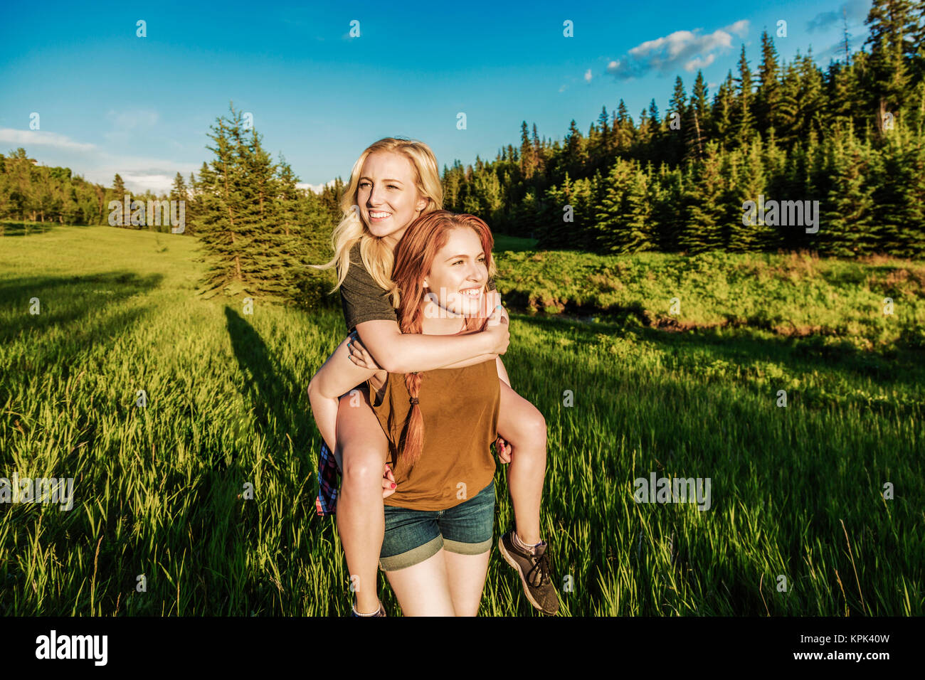 Two friends walking in a park, one giving the other a piggy back ride ...