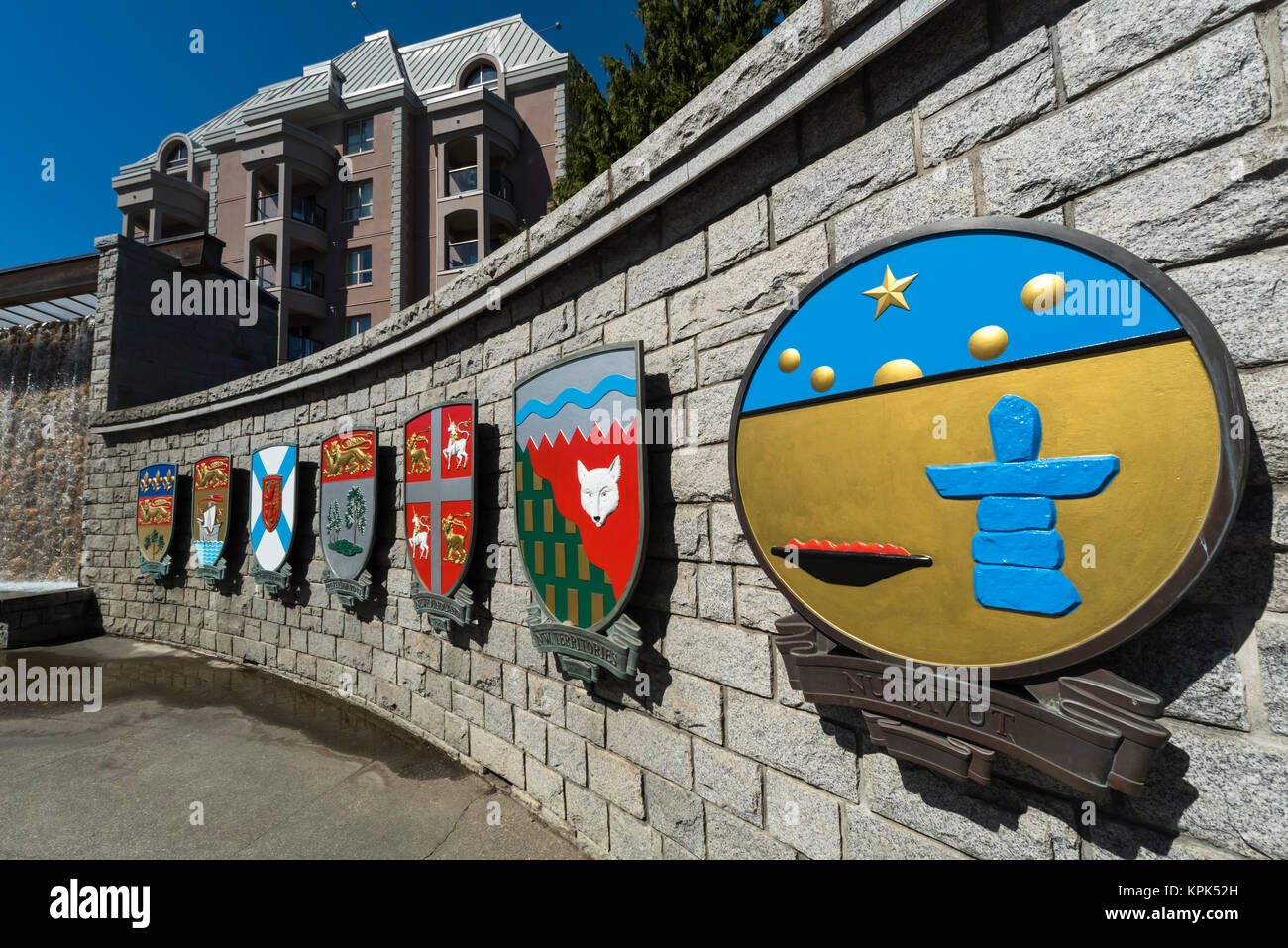Colourful symbolic crests and artwork on a stone wall along a walkway ...