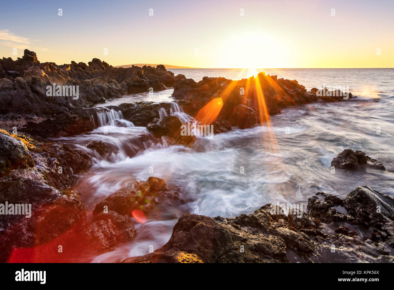 Dramatic sunset over the ocean with waterfalls along the rugged ...