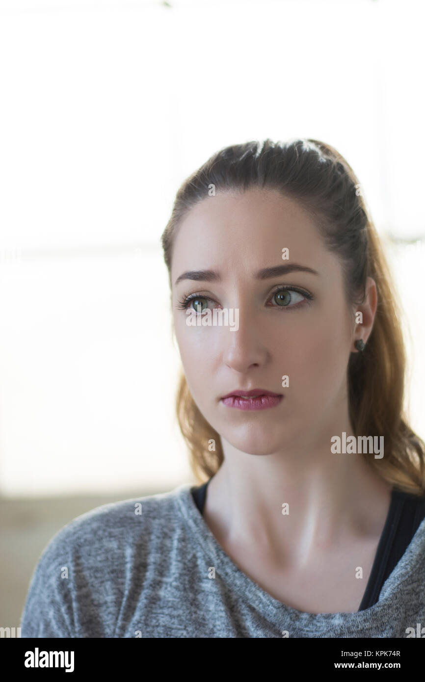 Worried young woman biting lips looking away Stock Photo - Alamy