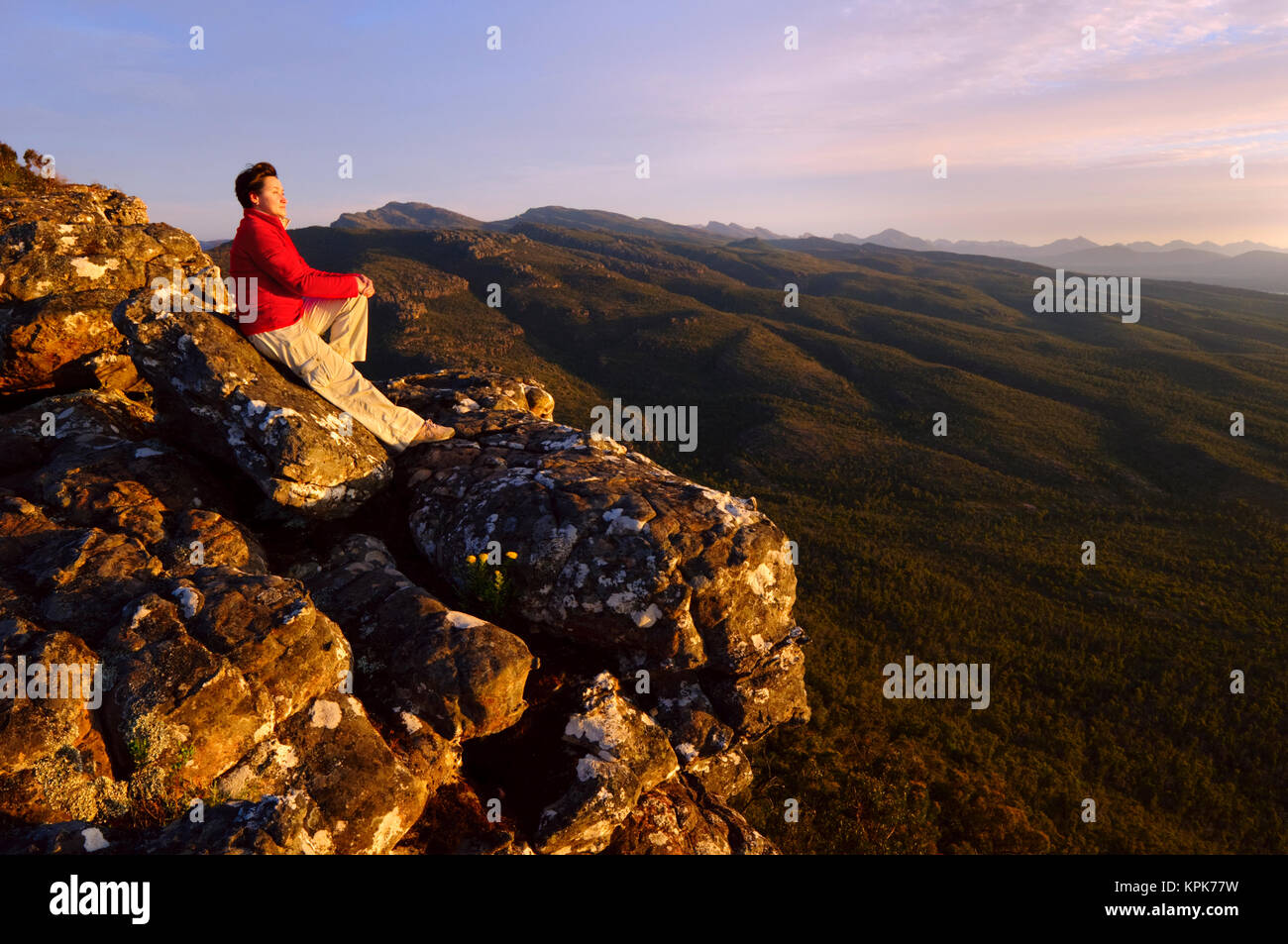 Adventurous woman sitting on a high cliff edge rock at the top of the ...