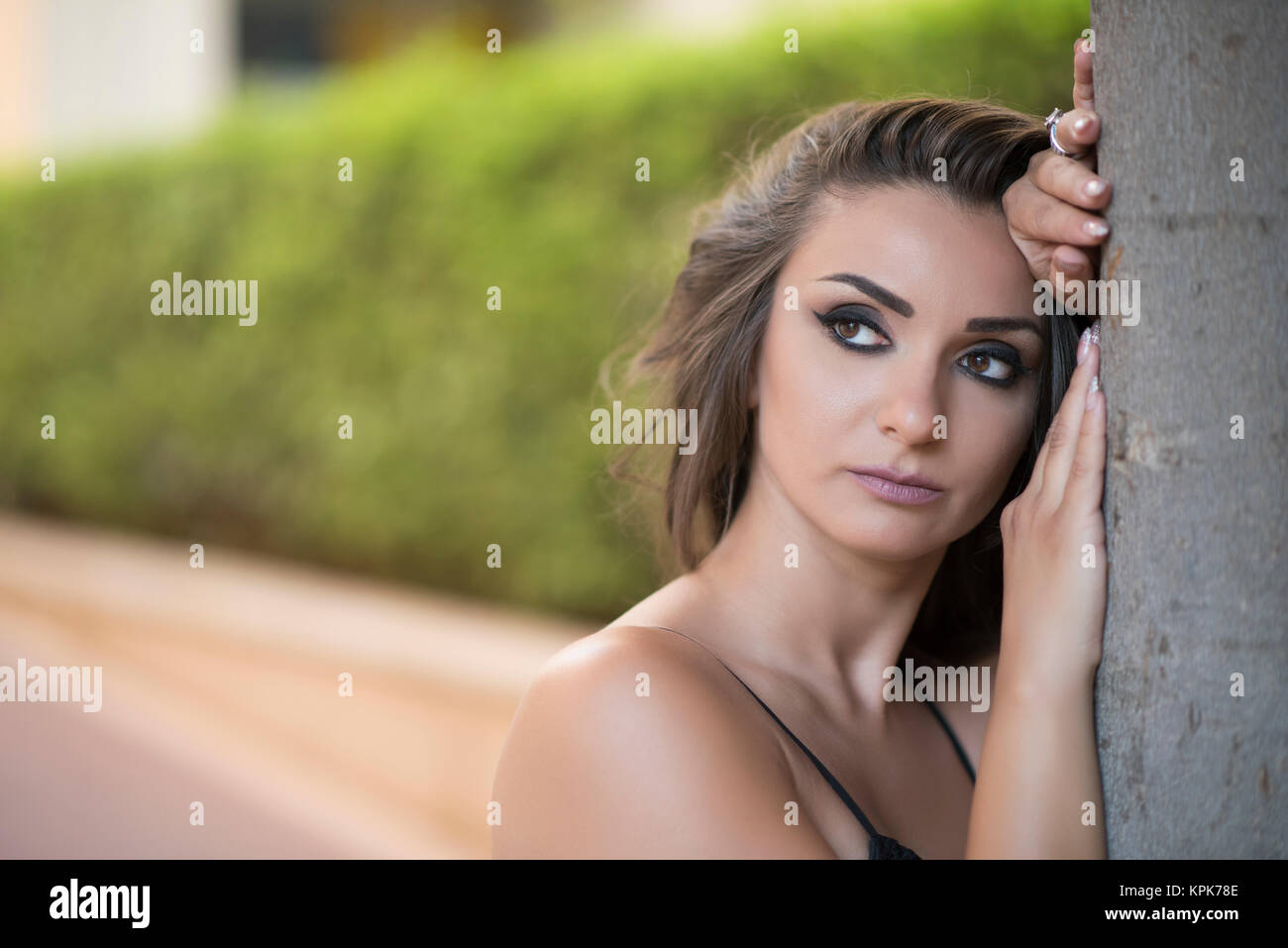 Beautiful woman leaning against a tree Stock Photo - Alamy