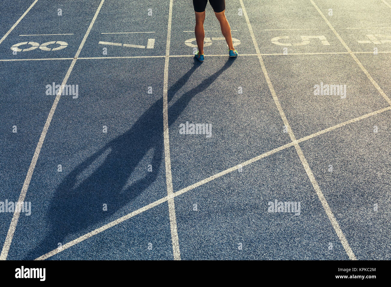 Rear view of legs of athlete standing on an all-weather running track ...