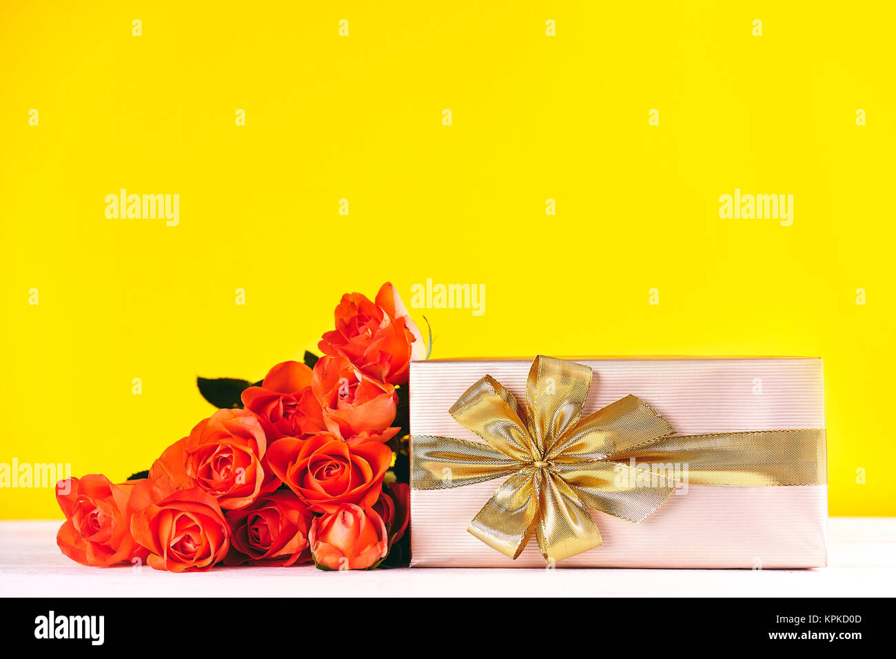 Bunch of orange roses and golden gist box on bright yellow background ...