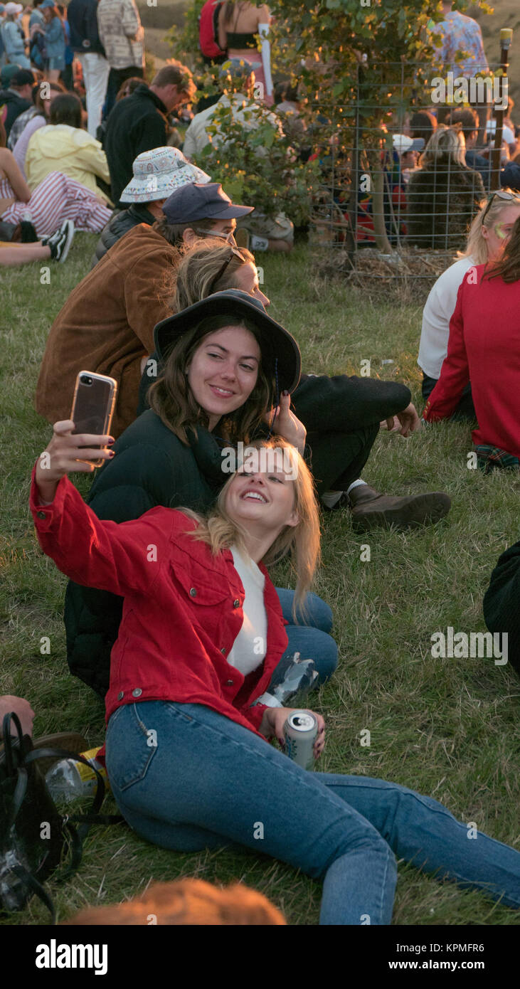 Two smiling colorfully dressed young women laying on the ground taking ...