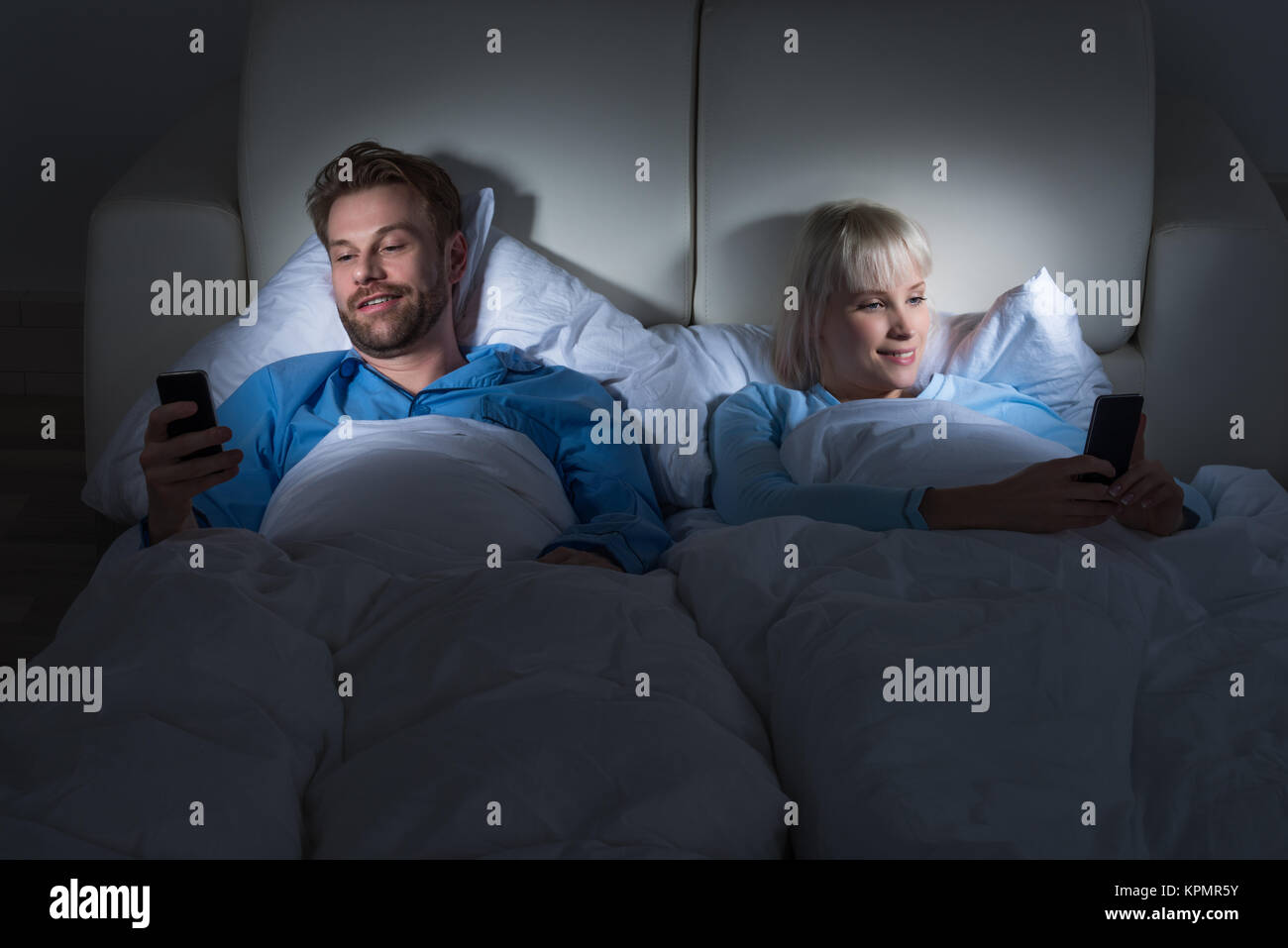 Couple Holding Mobile Phones In Bedroom Stock Photo - Alamy