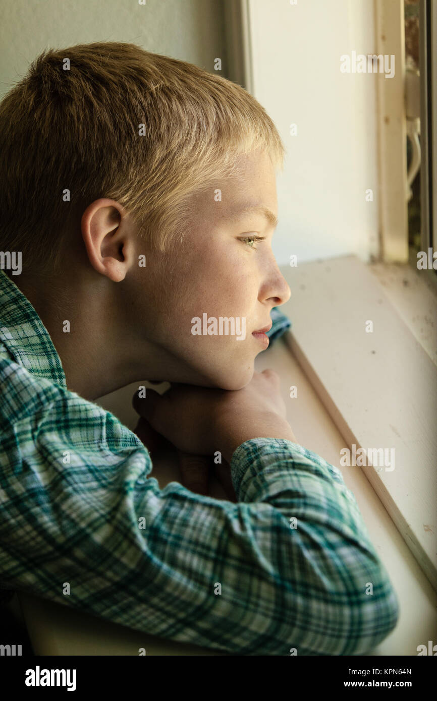 Child with sad expression sitting near window Stock Photo - Alamy